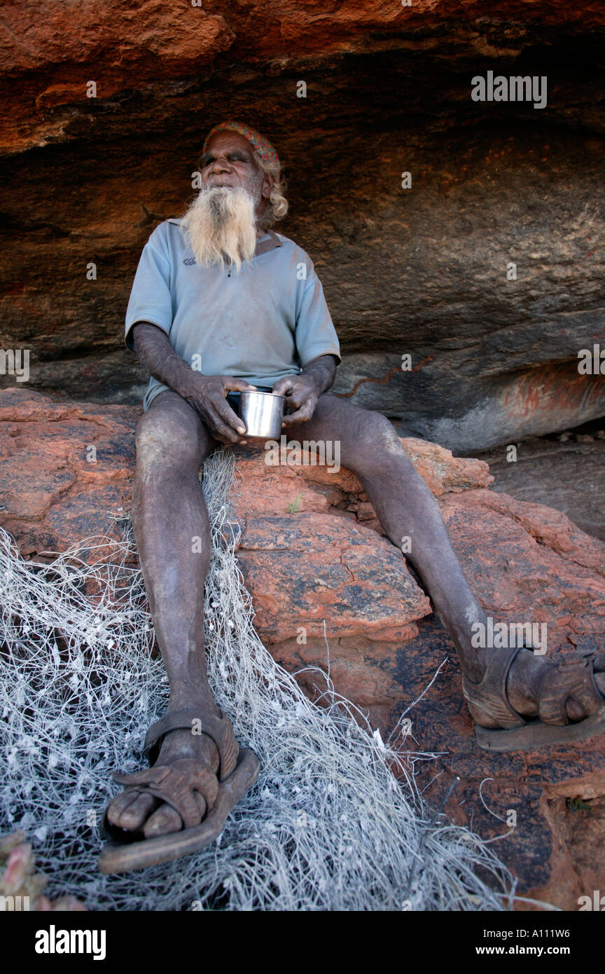 An aboriginal man sits next to the ancient aboriginal cave paintings of ...