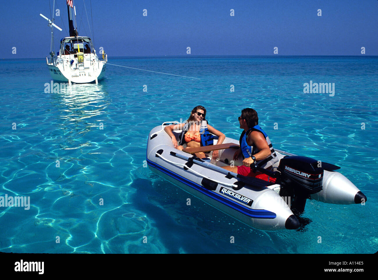 A SMALL INFLATABLE BOAT APPROACHES A SAILBOAT AT ANCHORAGE IN THE ...