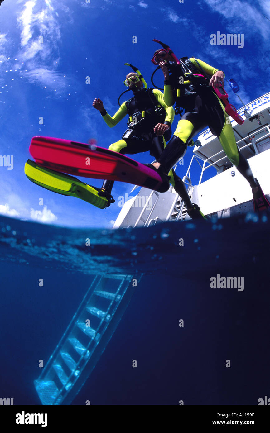 A MALE AND FEMALE SCUBA DIVER TAKING A GIANT STRIDE INTO THE WATER FROM ...