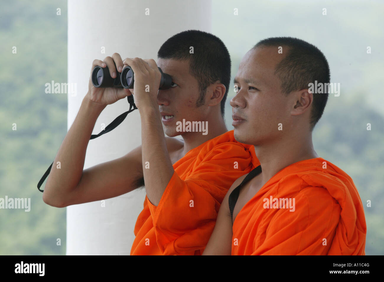 Two Monks in saffron robes one looking through binoculars at Buddha at ...