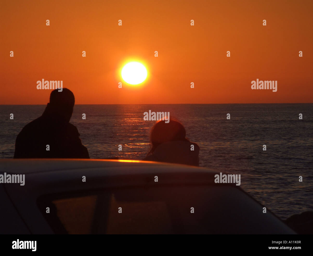 couple sitting watching beautiful red sunset Stock Photo - Alamy