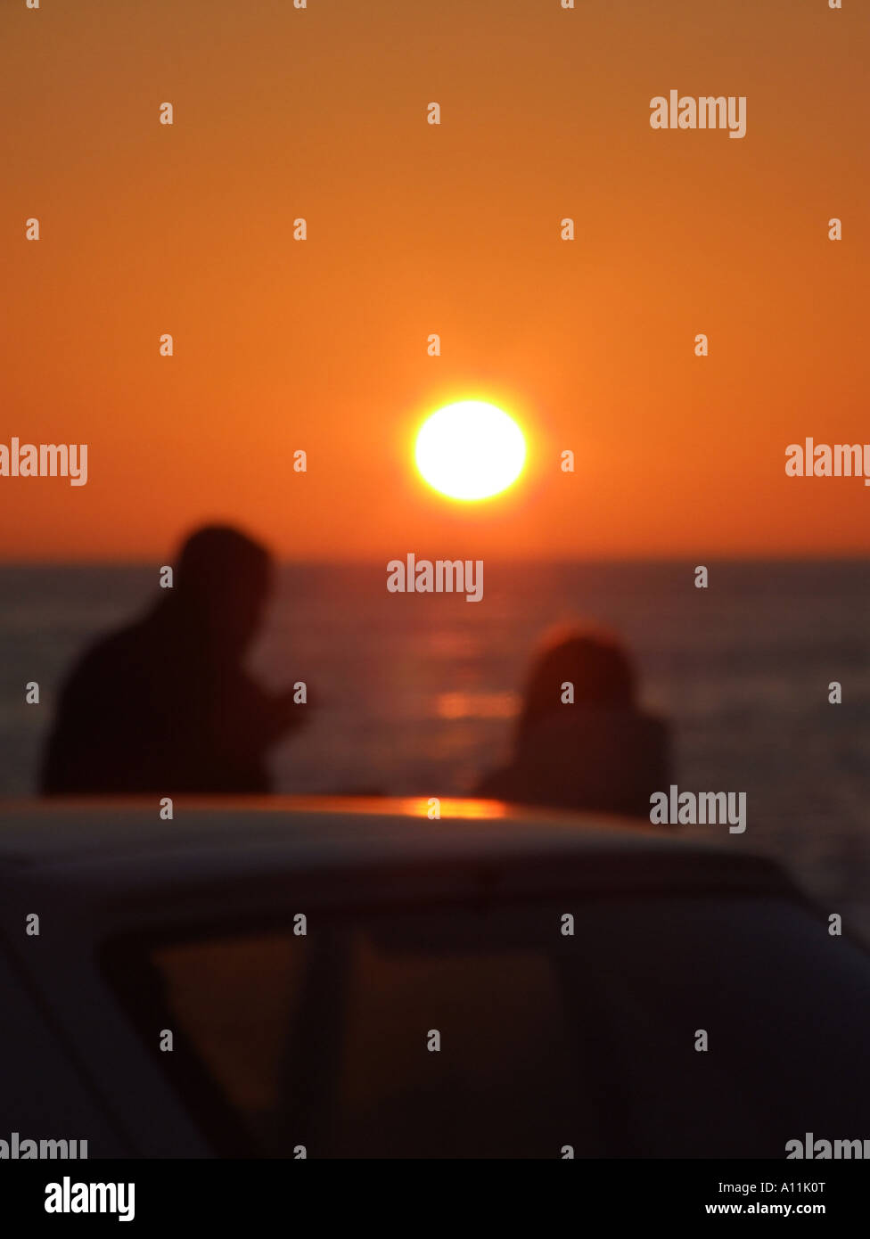 couple sitting watching beautiful red sunset Stock Photo - Alamy