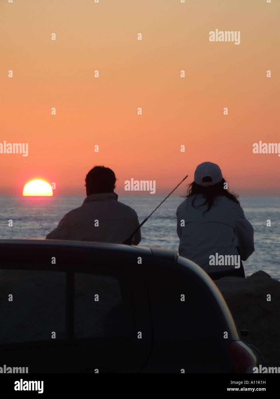 couple sitting watching beautiful red sunset Stock Photo - Alamy