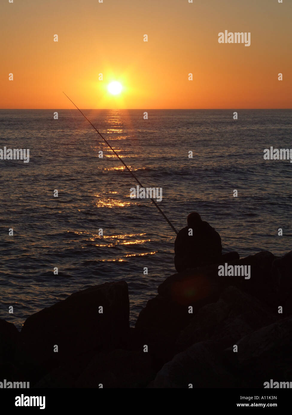 man fishing in sea with beautiful red sunset Stock Photo - Alamy