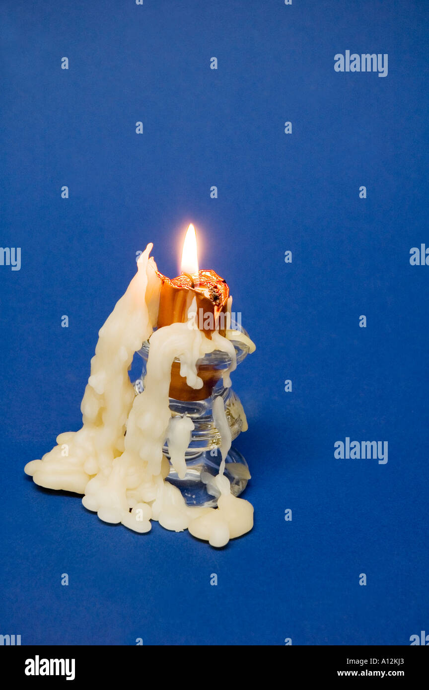 Seasonal candle with molten wax against plain dark blue background ...