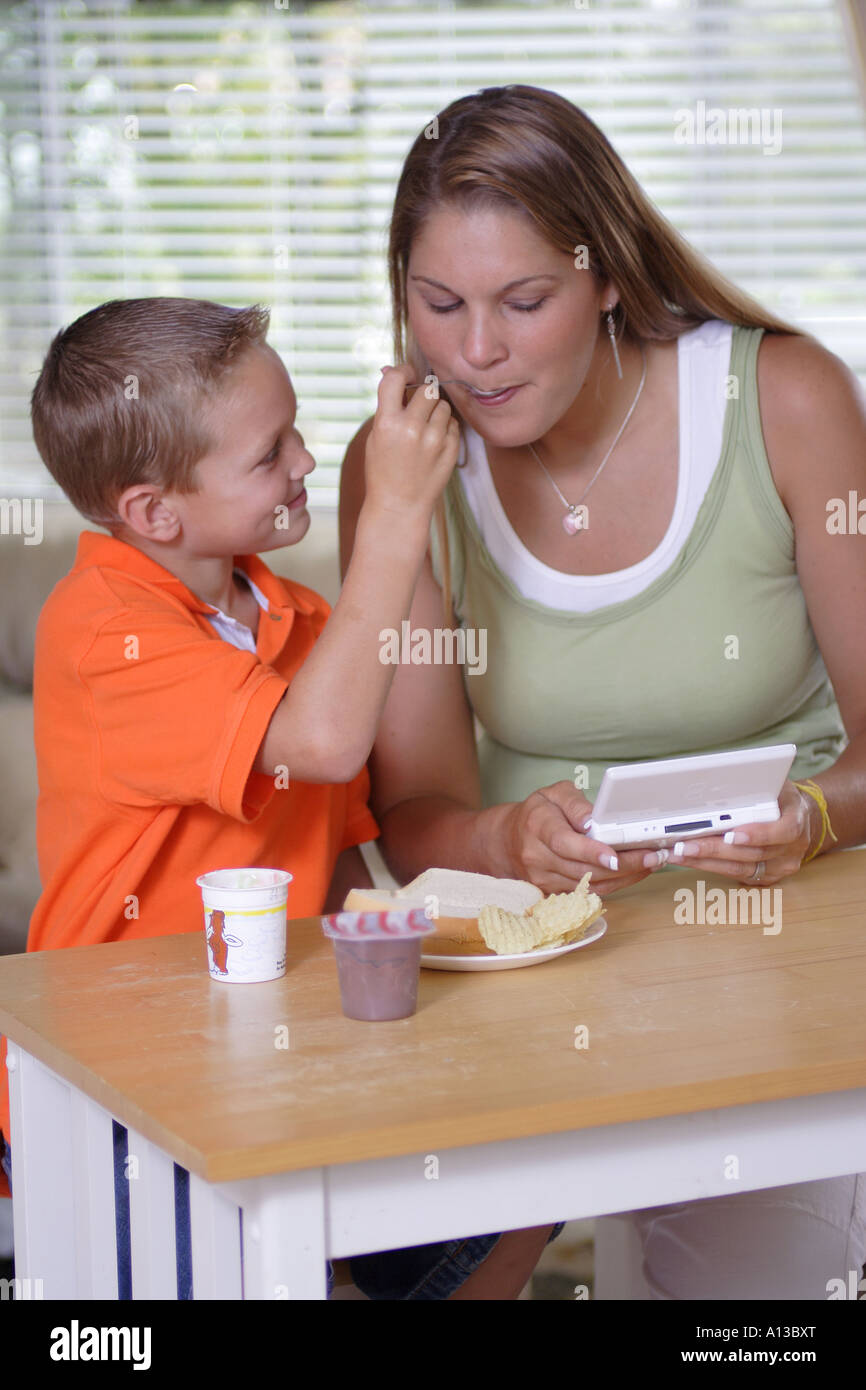 Boy feeds mom who is busy playing game Stock Photo - Alamy