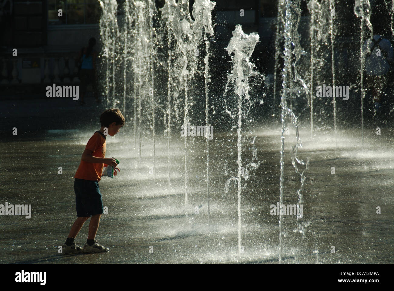 Young boy playing outdoors to dodge high water jets at play fountain ...