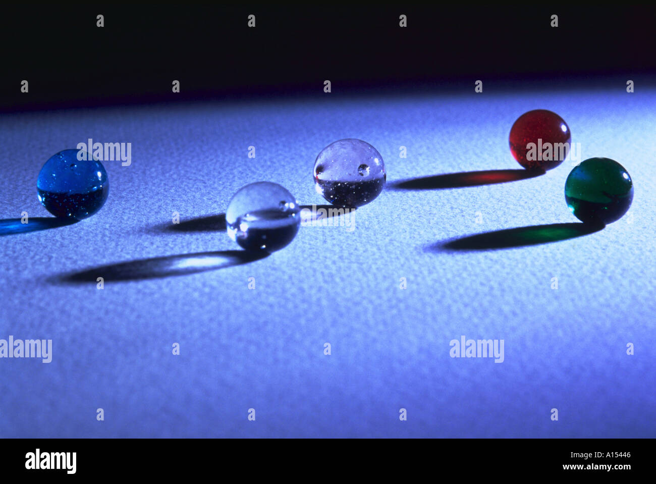 Five marbles cast shadows on a white surface One marble is blue two are ...