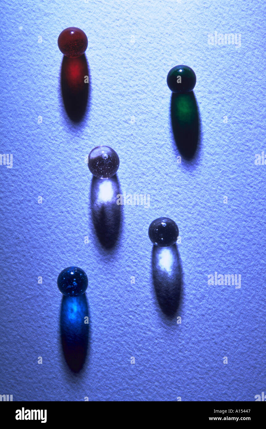 Five marbles cast shadows on a white surface One marble is blue two are ...