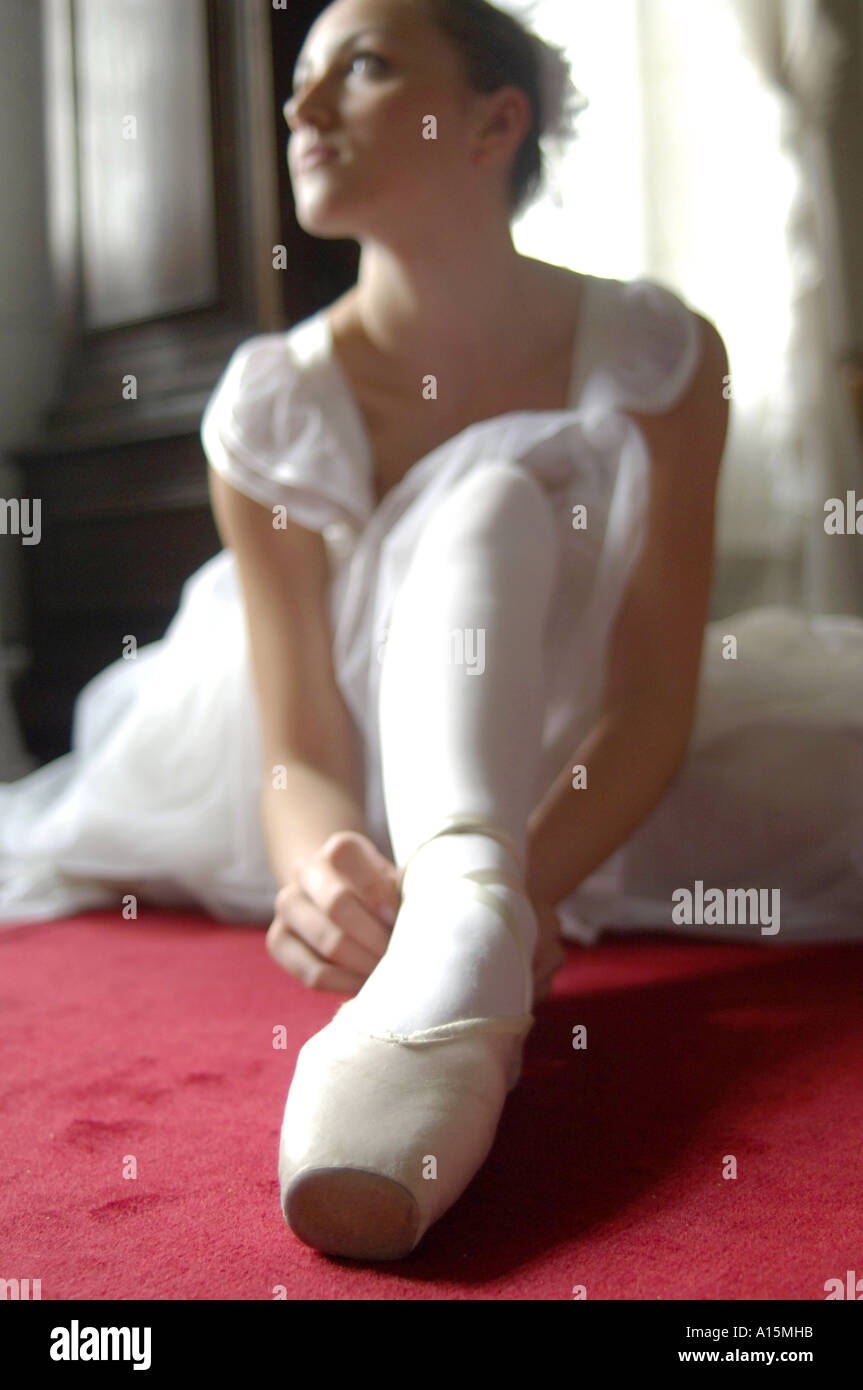 A ballerina tying the laces on her ballet shoe sitting on a red carpet ...