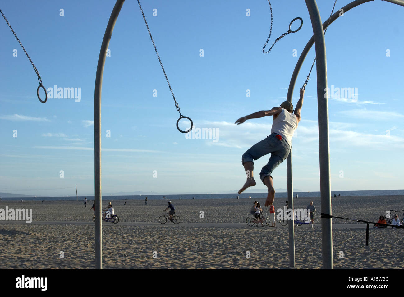 A young man swings from hoop to hoop at outdoor beach gymnastic center ...
