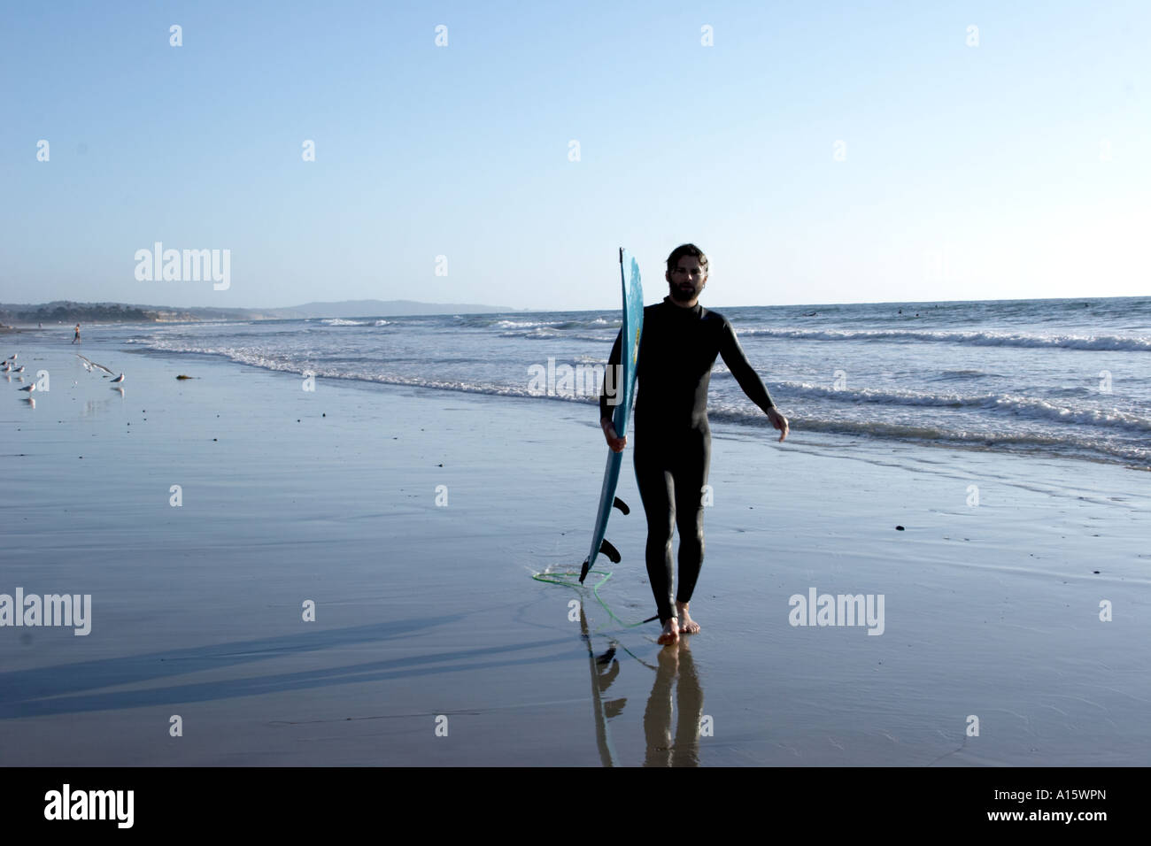 A young male surfer carries his board along the water edge after a ...