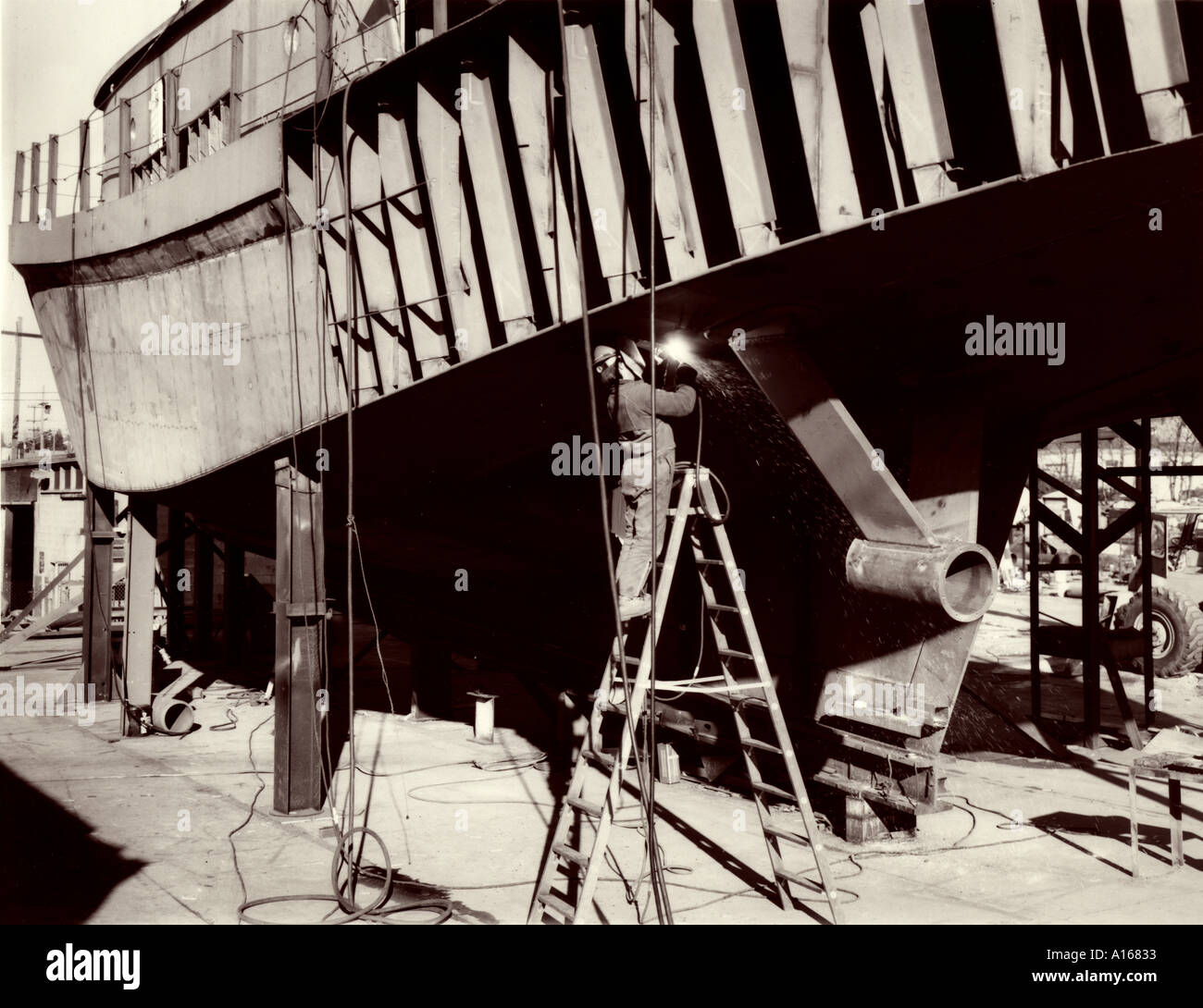 A man welding steel plates on the hull of a new tugboat under ...