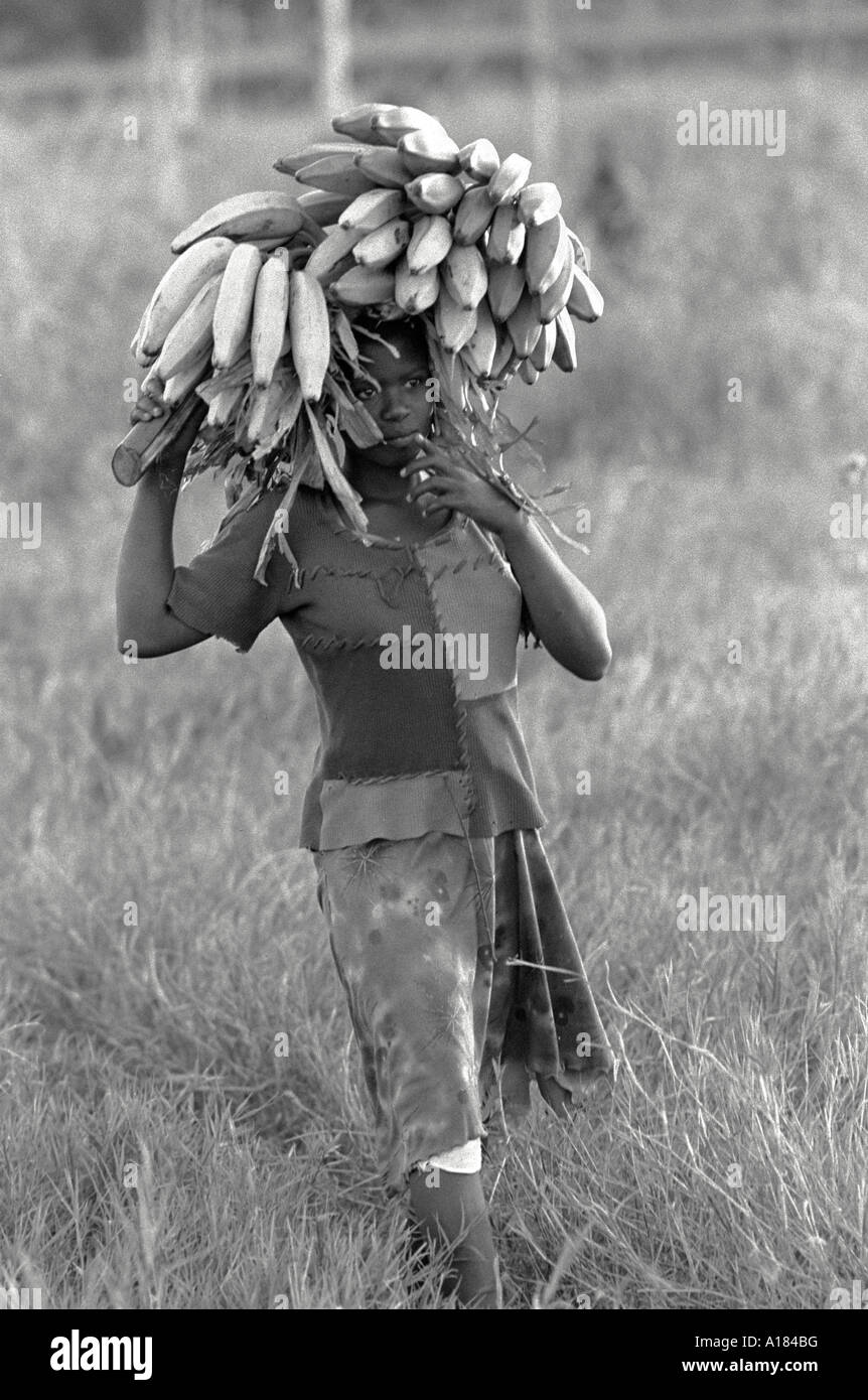 B/W of a young woman carrying a hand of bananas on her head. Kakoneni ...