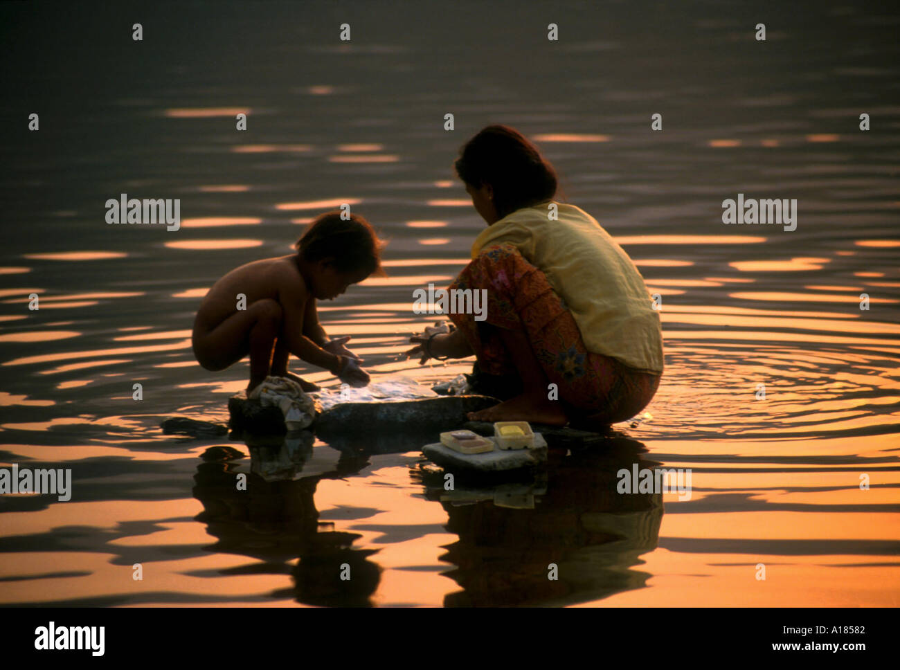 Mother and child silhouetted at dusk washing clothing in Phewa Tal ...