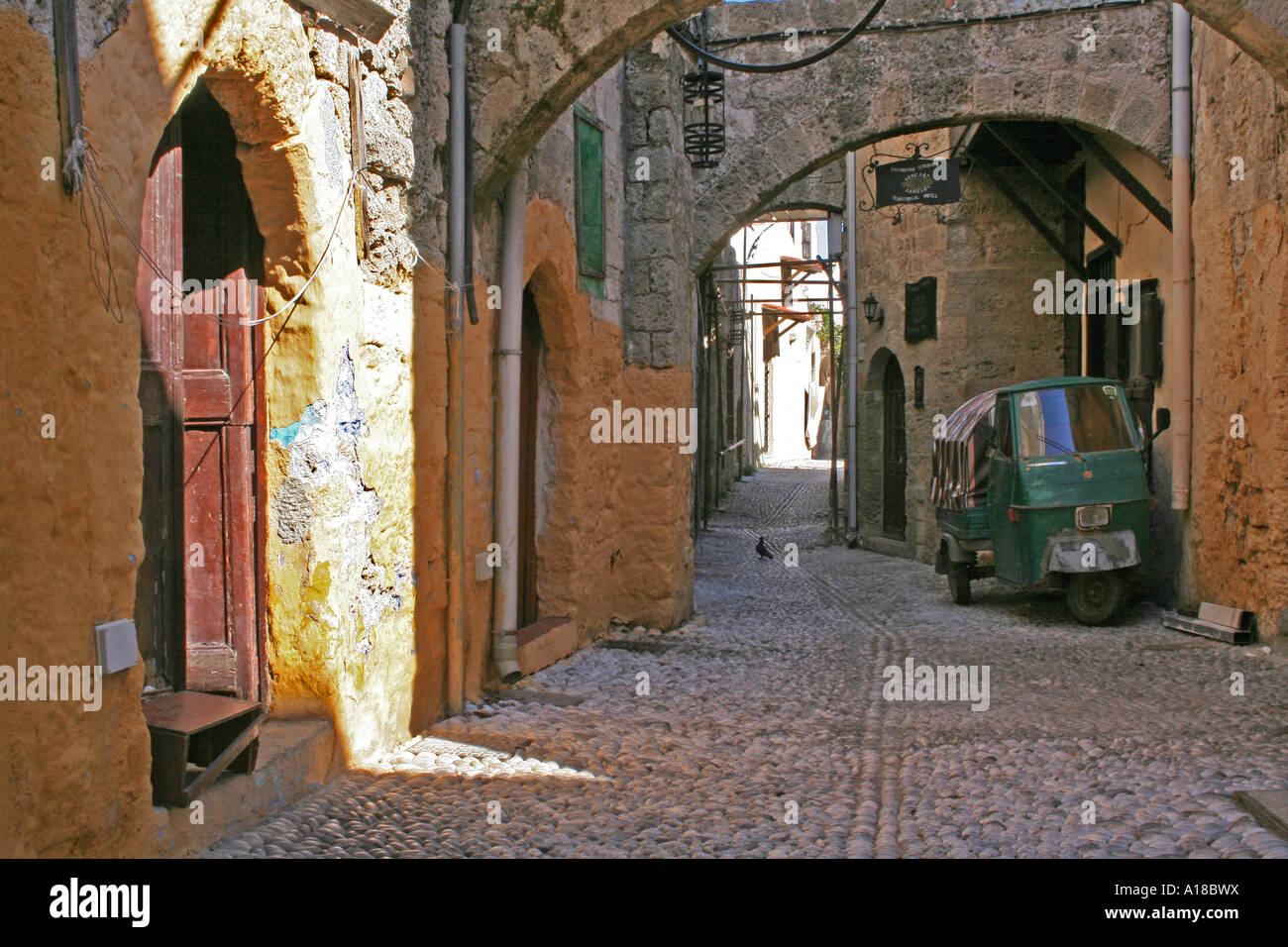 Small, Greek back street with ray of sunlight casting down on house ...