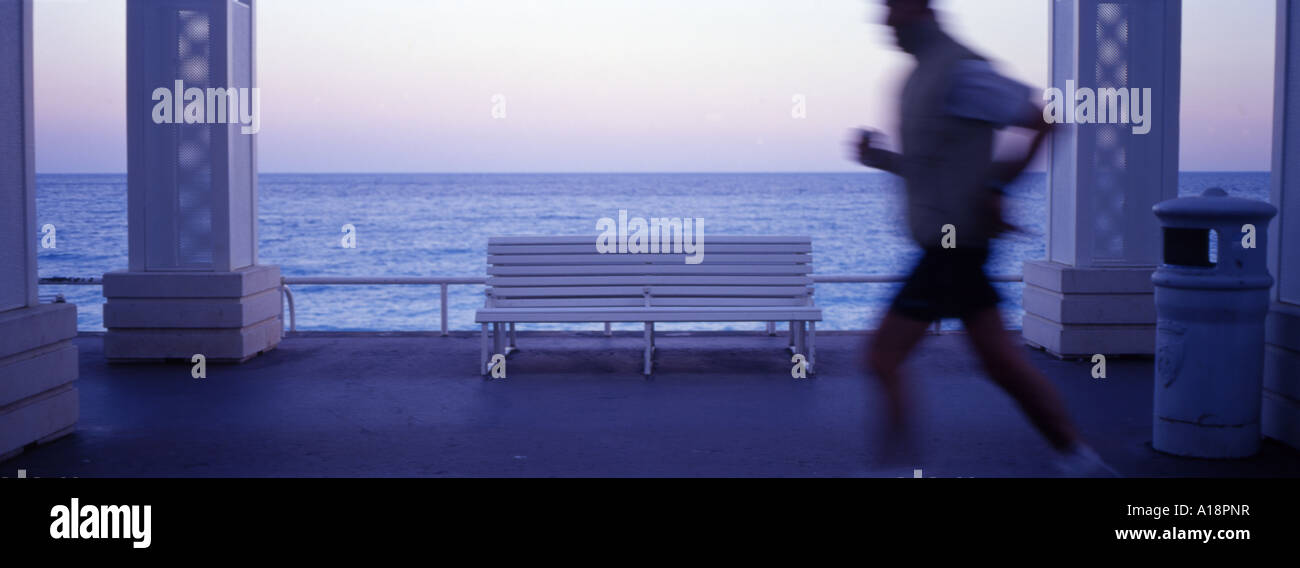 Panoramic image of a man jogging past a seafront bench at dusk on the ...