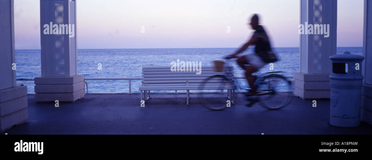 Panoramic image of a man cycling past a seafront bench at dusk on the ...