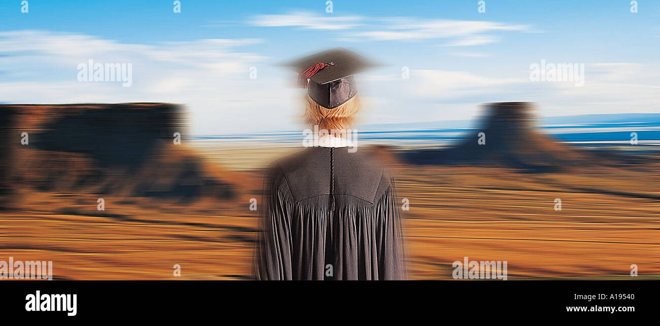 College graduate in cap and gown looking out onto the horizon as the ...