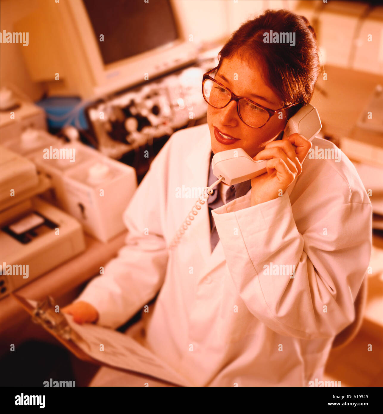 Female laboratory technician talking on the phone while looking at a ...
