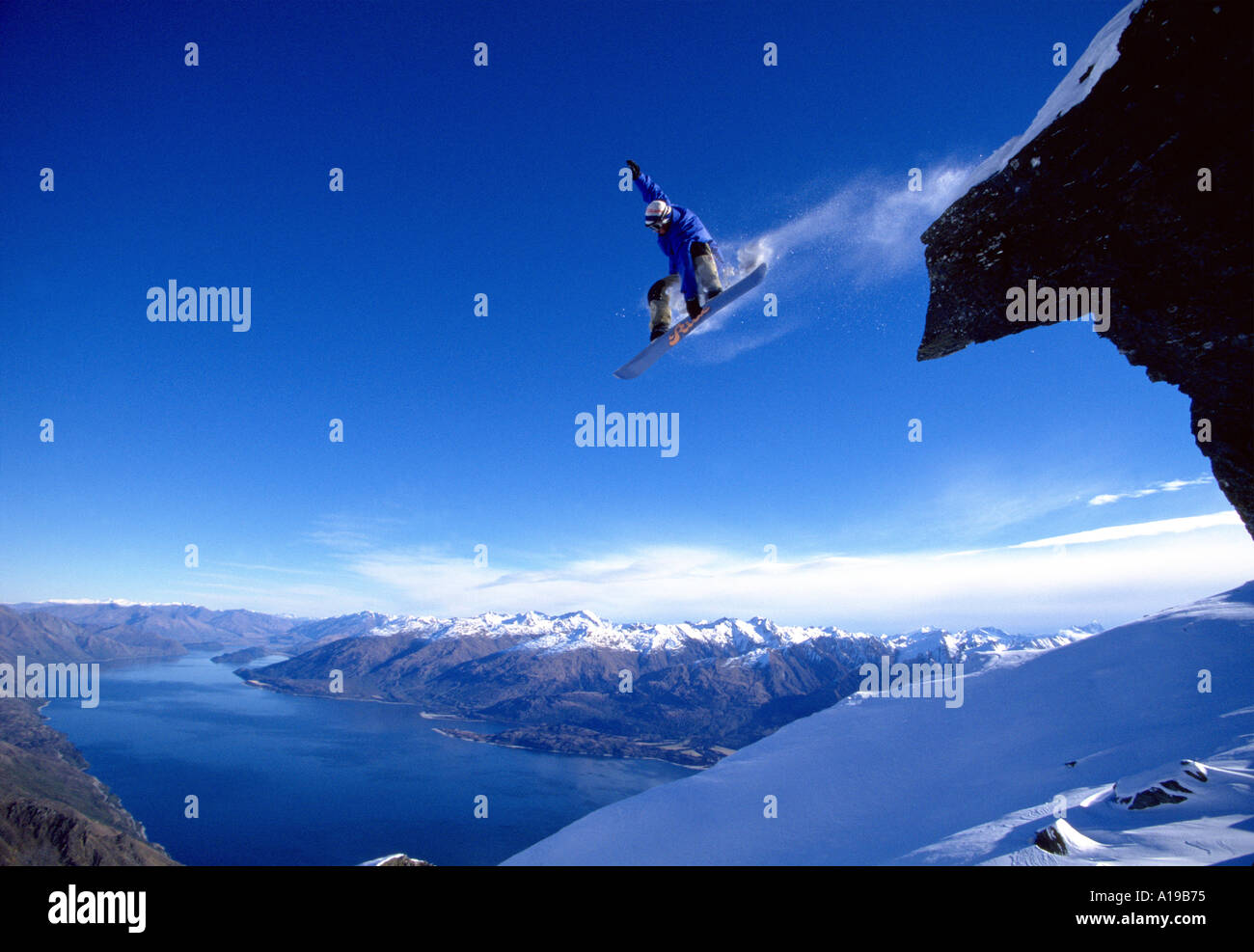 Snowboarder taking massive air off a cliff with lakes and mountains ...