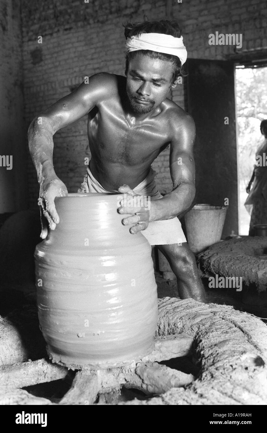 B/W of a potter turning a large pot on a primitive wheel turned by hand ...