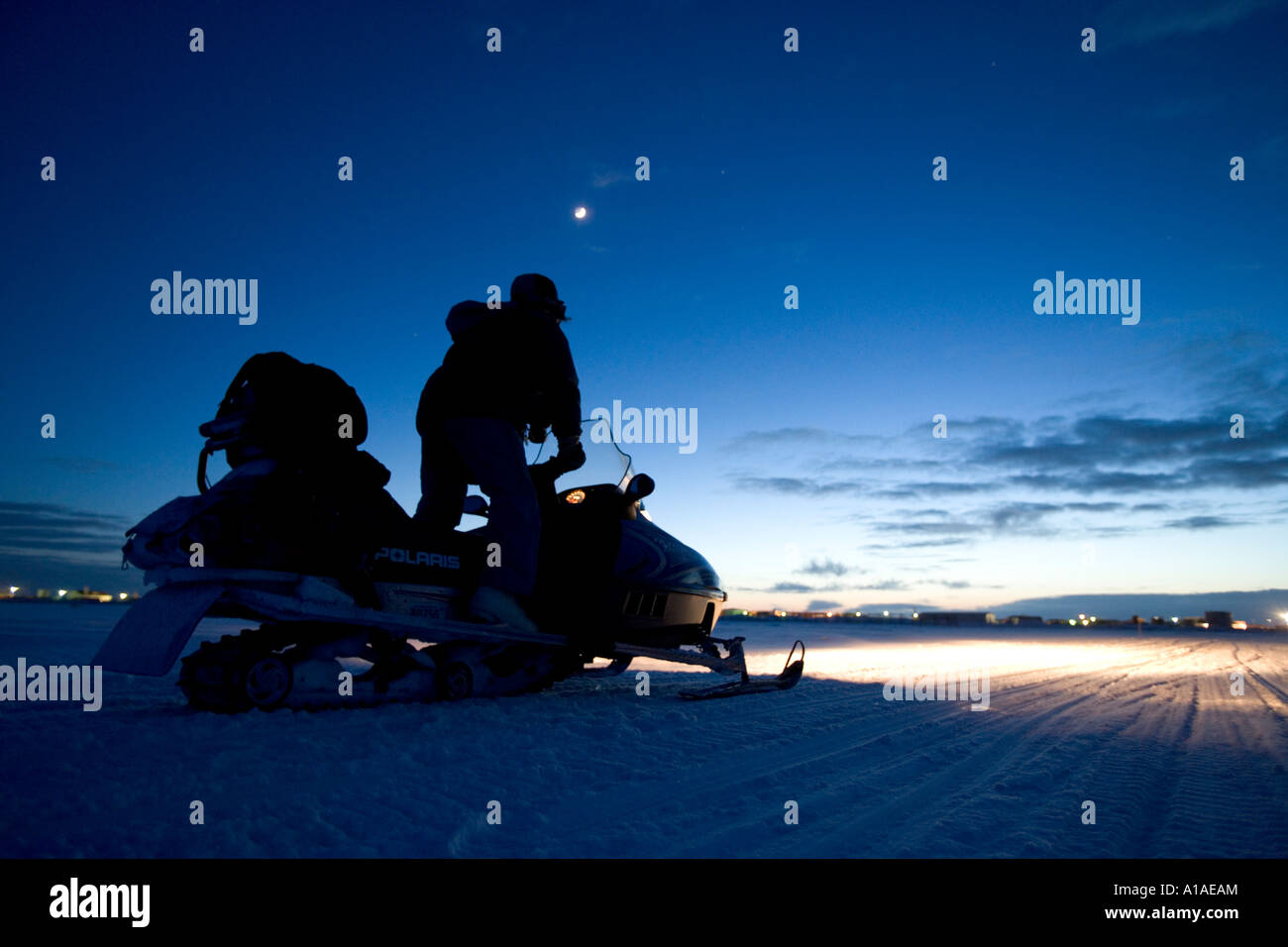 USA Alaska Unalakleet Man rides snowmobile on sea ice under crescent ...