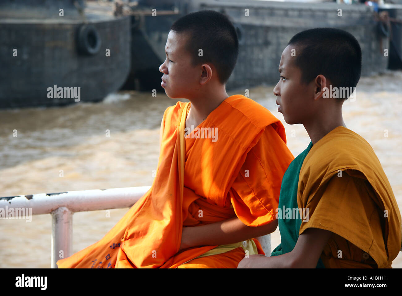 Two young buddhist monks watch a passing ship from a river ferry in ...