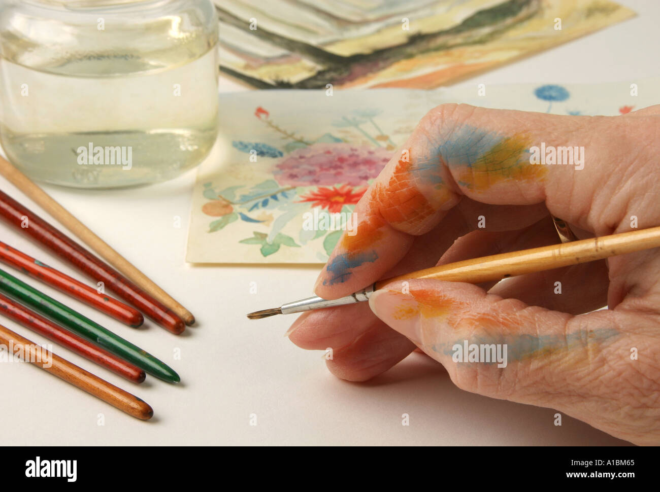 An artists hand with brushes paintings and water Stock Photo - Alamy
