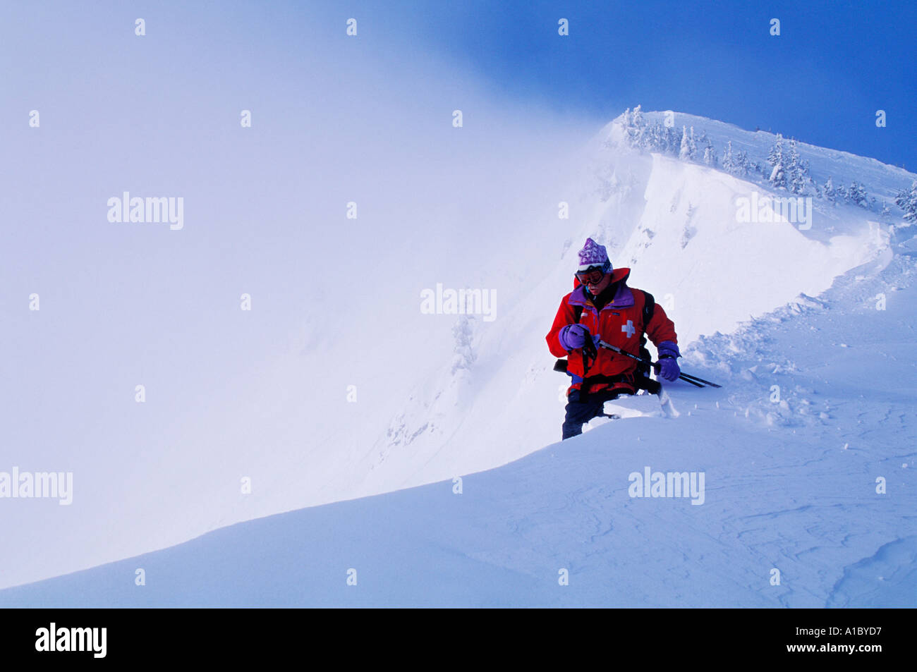A ski patrolman cuts a cornice with his ski poles to prevent snow ...