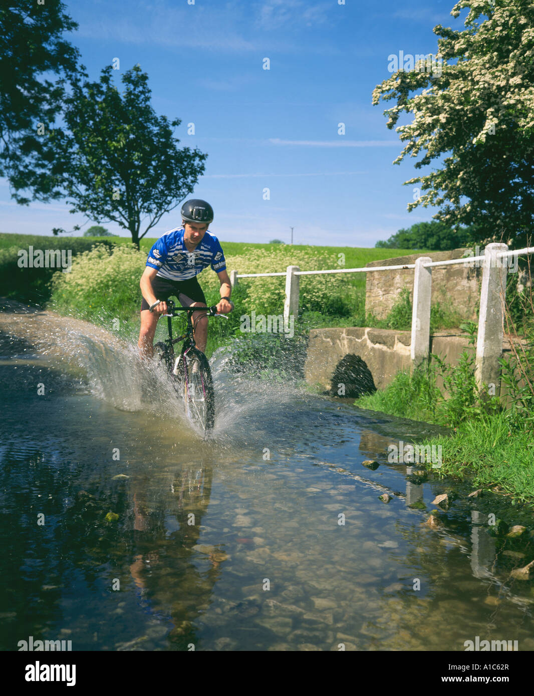 mountain biker riding bike through stream in the village of thorner ...