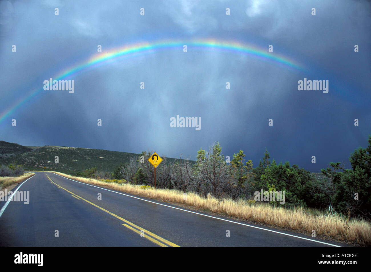 rainbow over country road during rain storm in the high mountains of ...