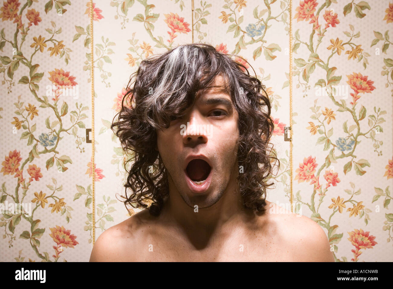 Side profile of a man with long curly hair against flowery wallpaper ...