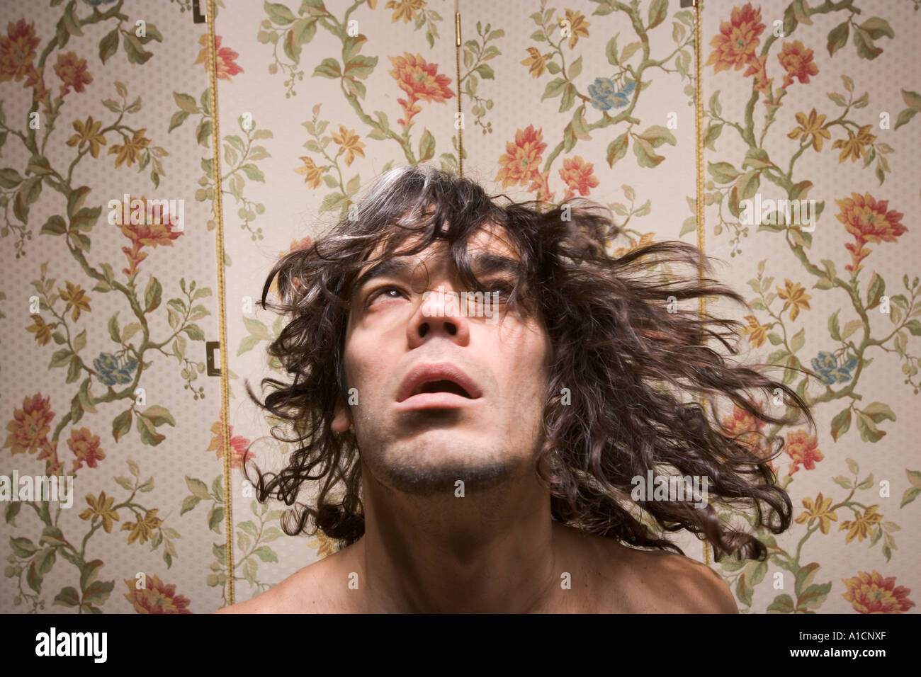 Side profile of a man with long curly hair against flowery wallpaper ...