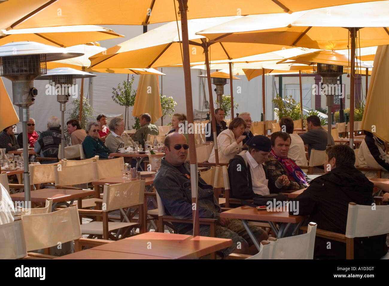 People eating at pavement restaurant with yellow parasols oven wooden ...