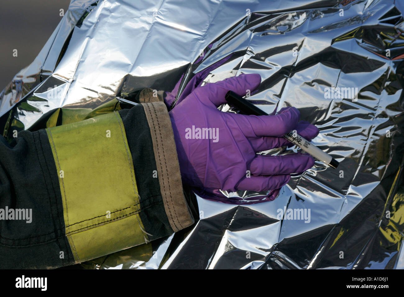 An EMT has his hand on patient under a silver emergency blanket at a ...