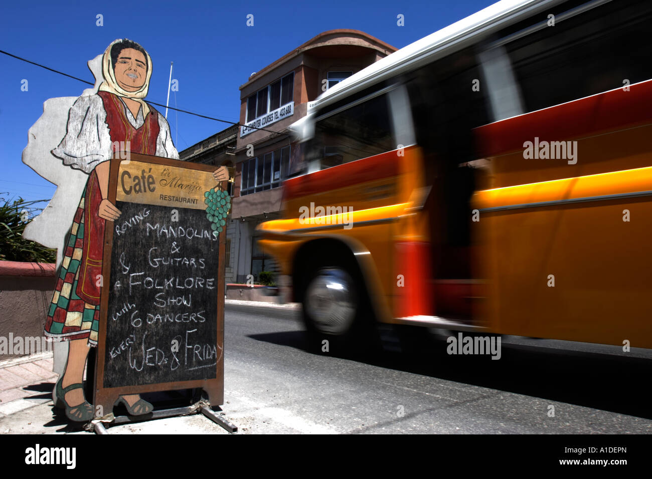 A yellow bus passes a restaurant menu board in Mosta, Malta Stock Photo ...