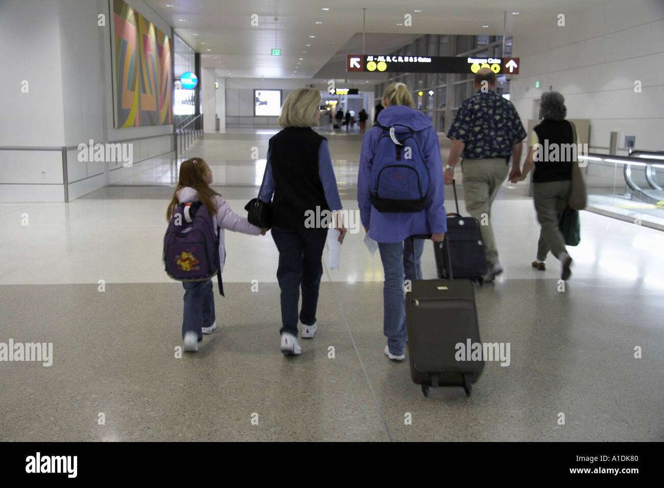 People holding hands and pulling luggage through airport concourse ...