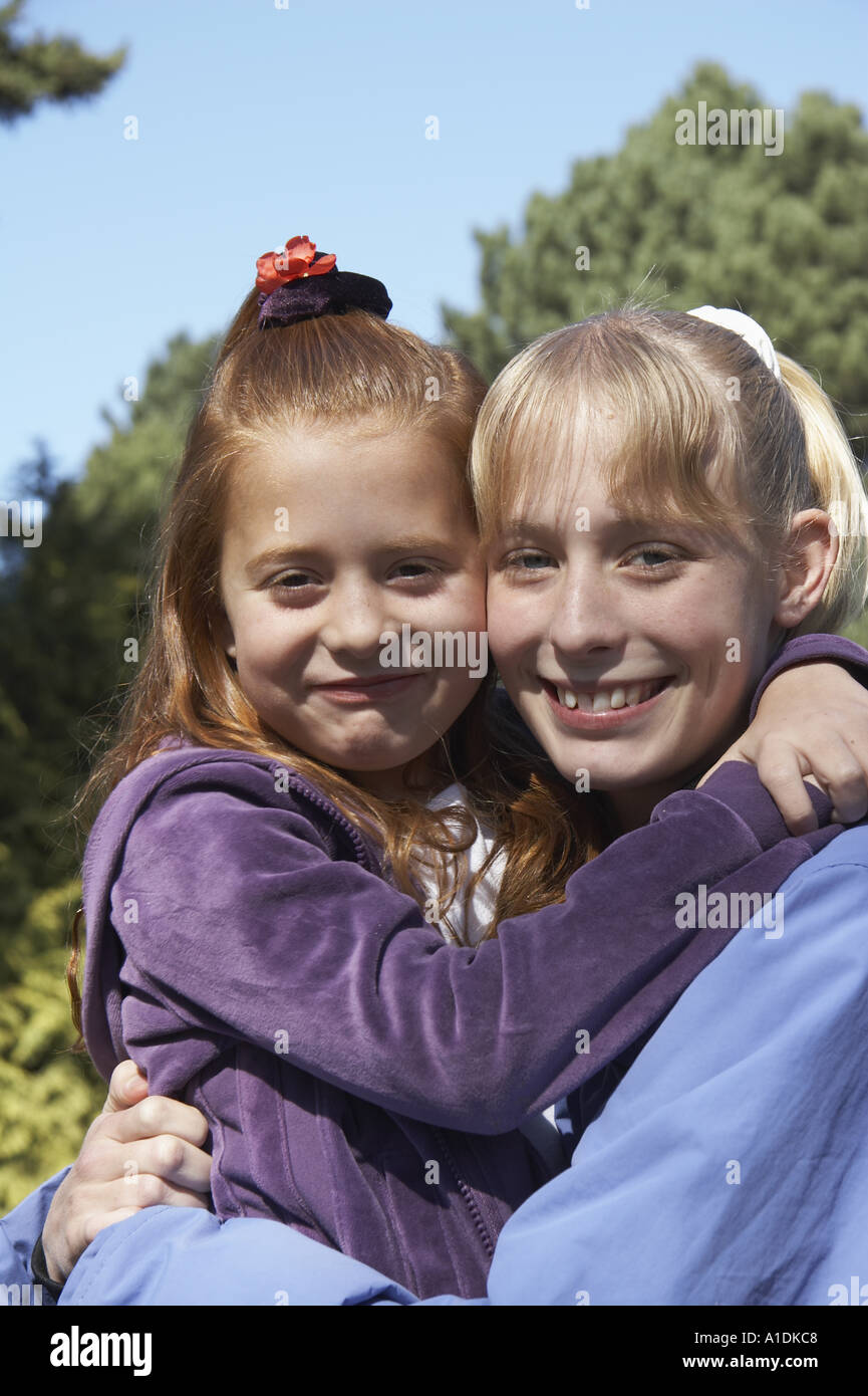 Sisters with arms wrapped around each other hugging cheek to cheek ...