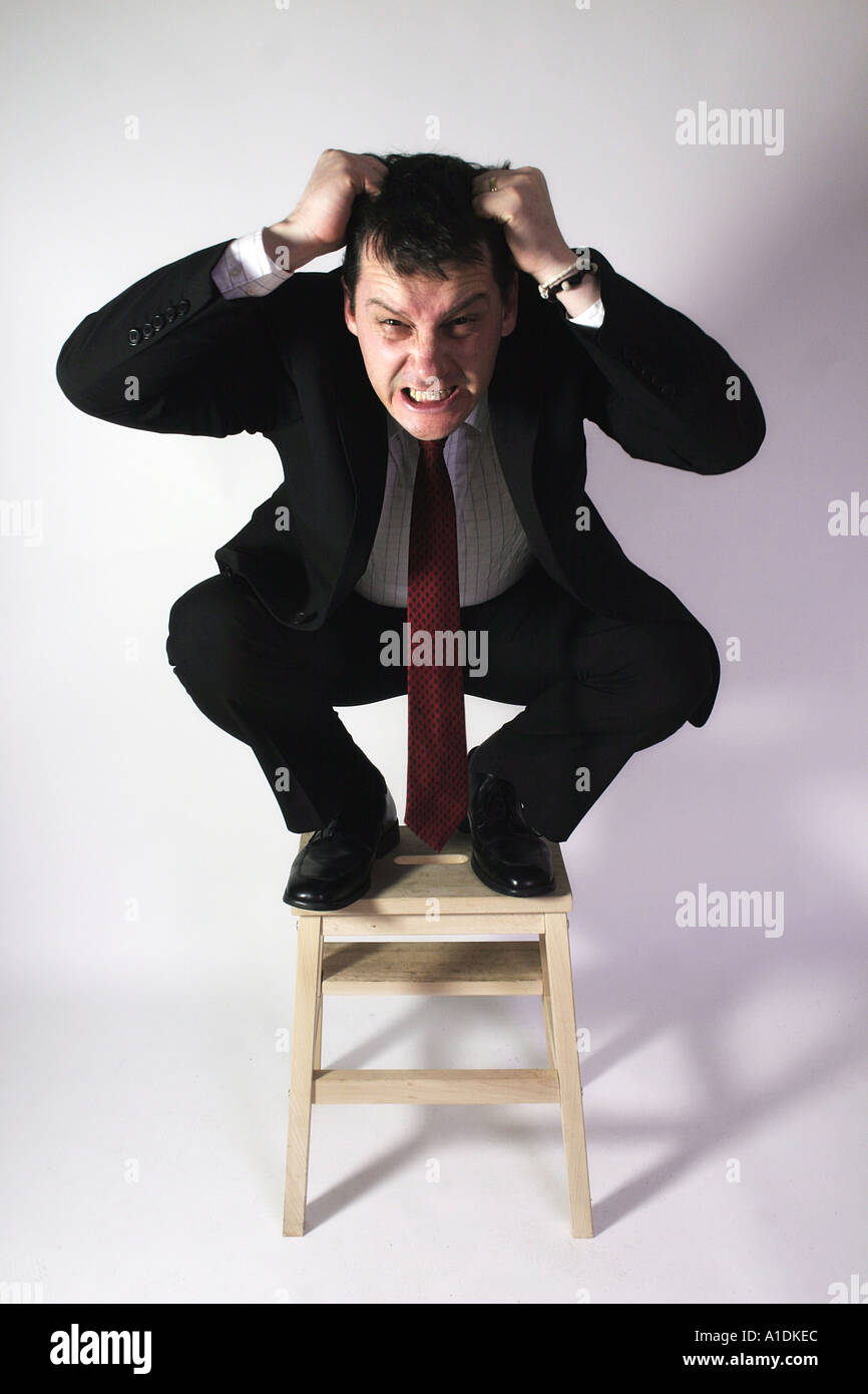 Business man crouched on a stool looking angry and stressed Stock Photo ...