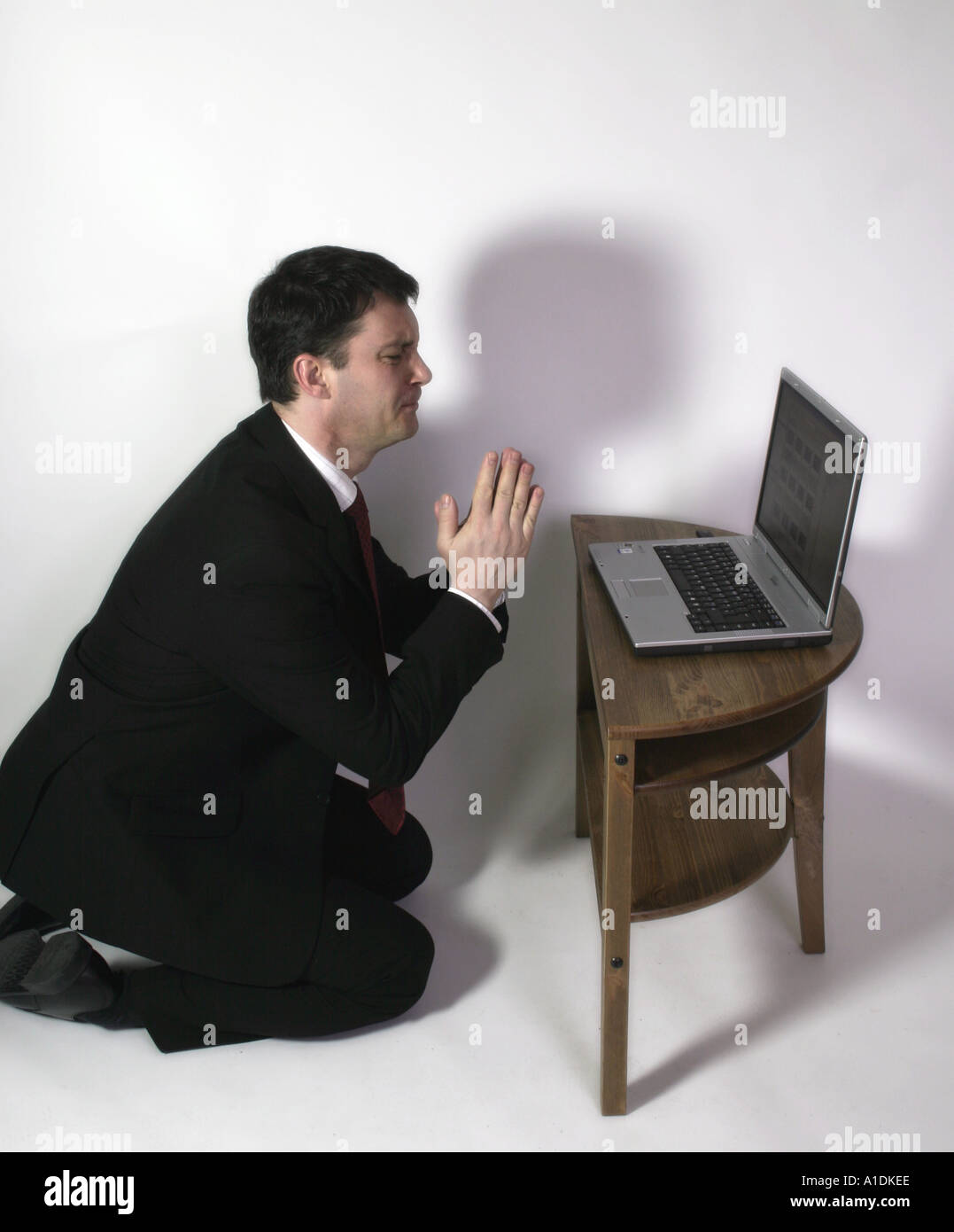 Business man kneeling praying to his laptop computer Stock Photo - Alamy