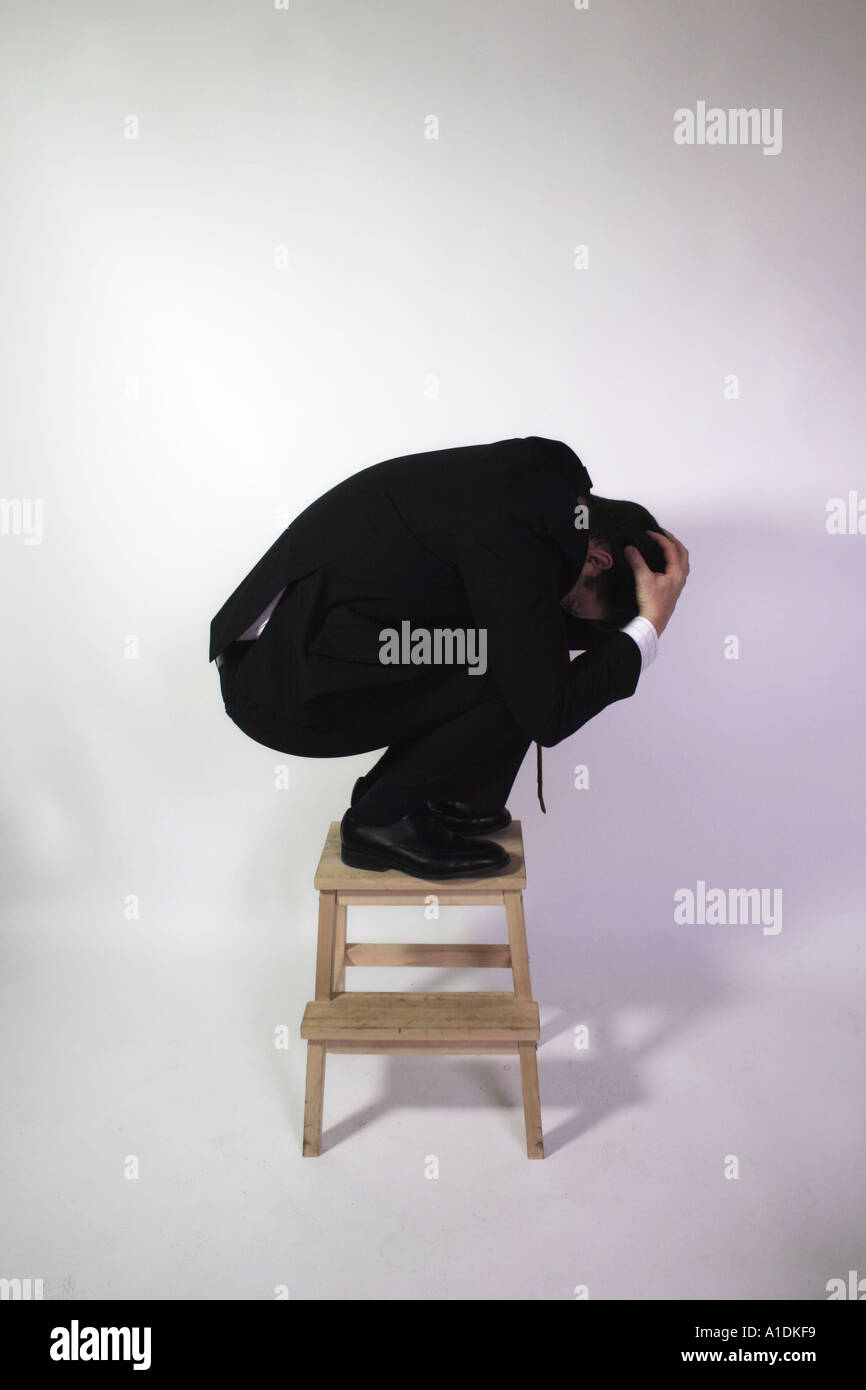 Man in suit crouching on top of a stool Stock Photo - Alamy