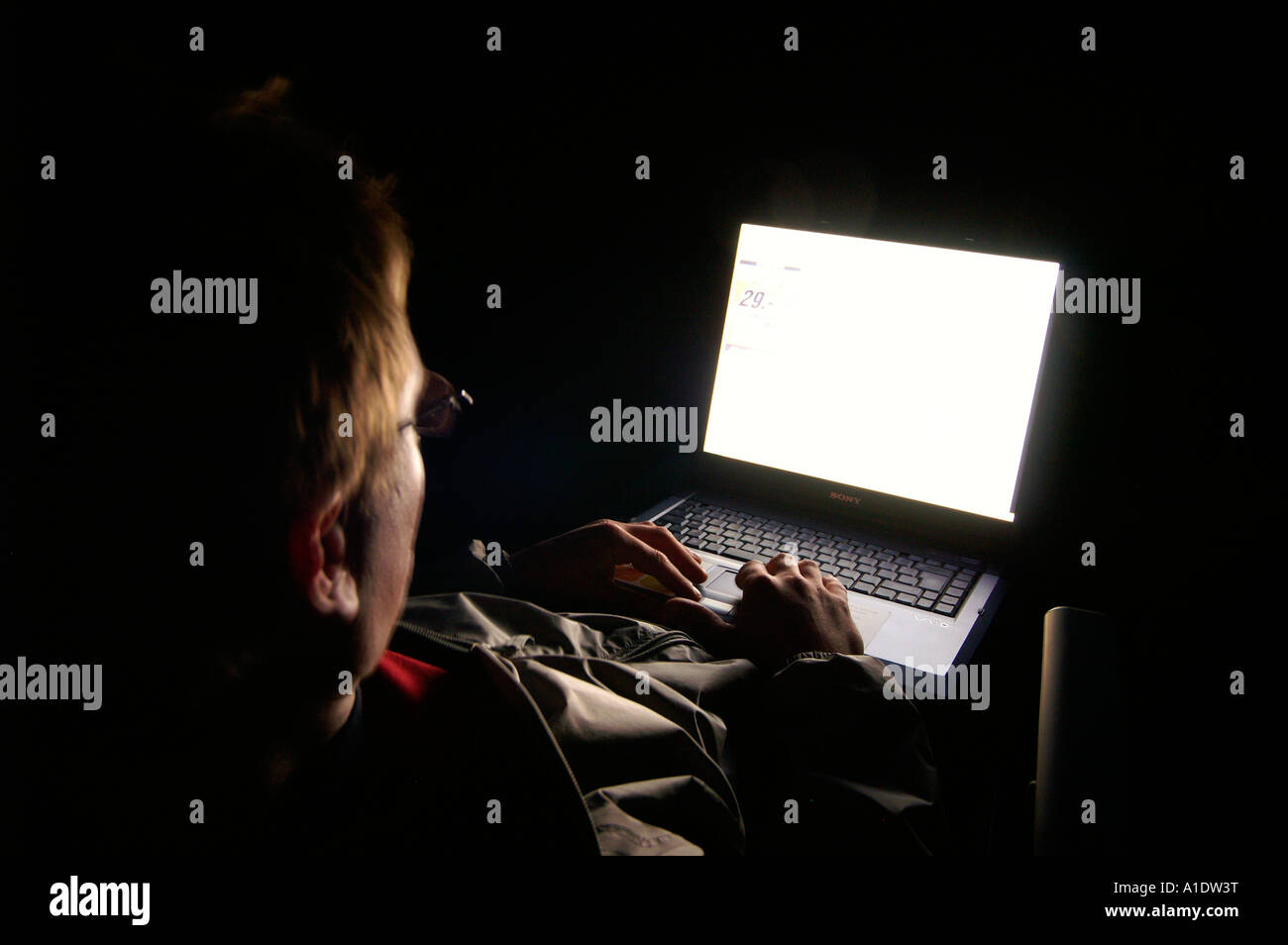 Man in dark night, face lit by blank white LCD laptop display light ...
