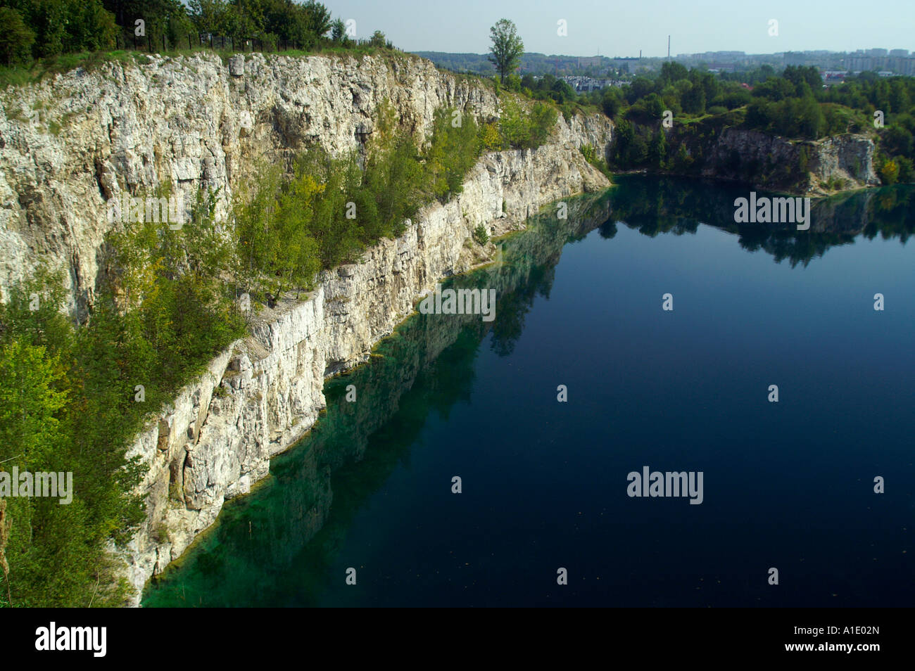 Abandoned flooded stone pit quarry with clear blue water pool in centre ...
