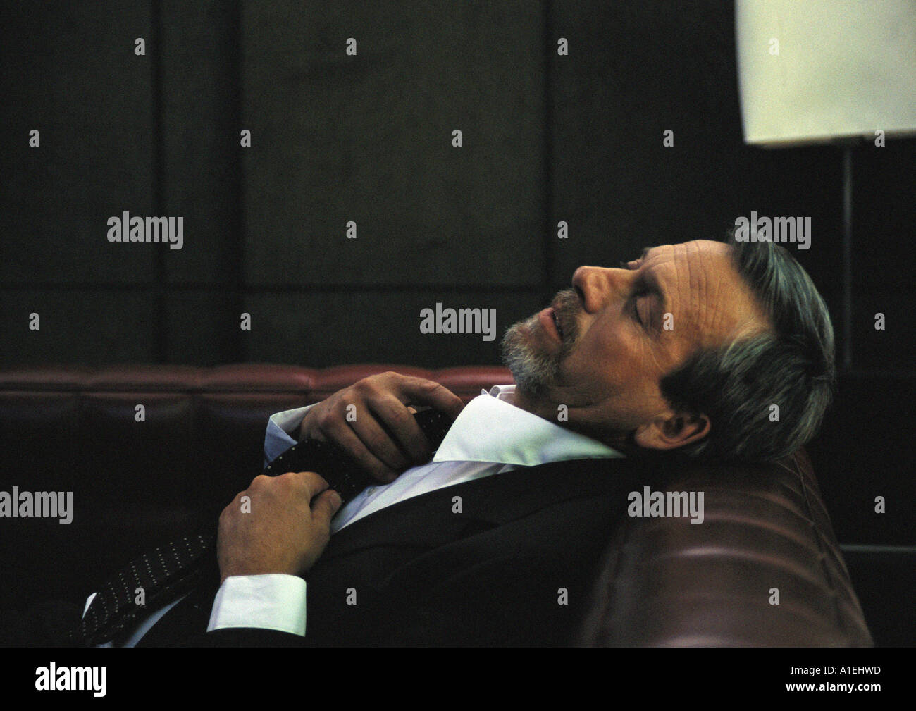 Businessman leaning head on back of sofa and adjusting tie Stock Photo ...