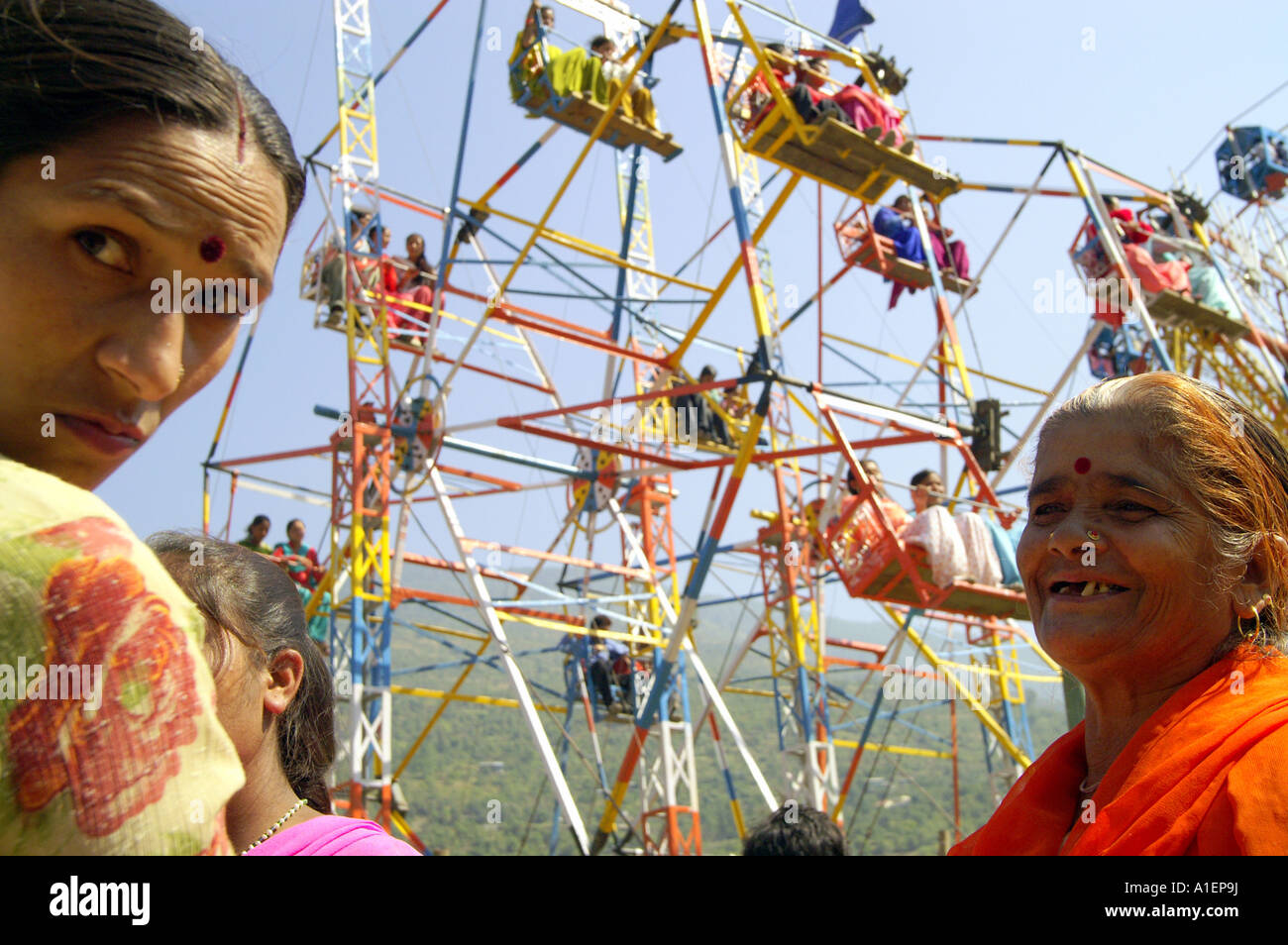 Two old indian ladies smiling in front of Indian merry go round giant ...