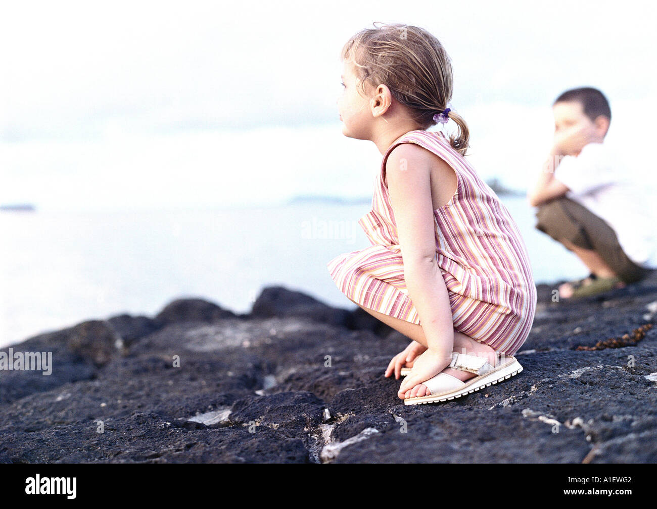 Two children crouching on rocks near sea Stock Photo - Alamy