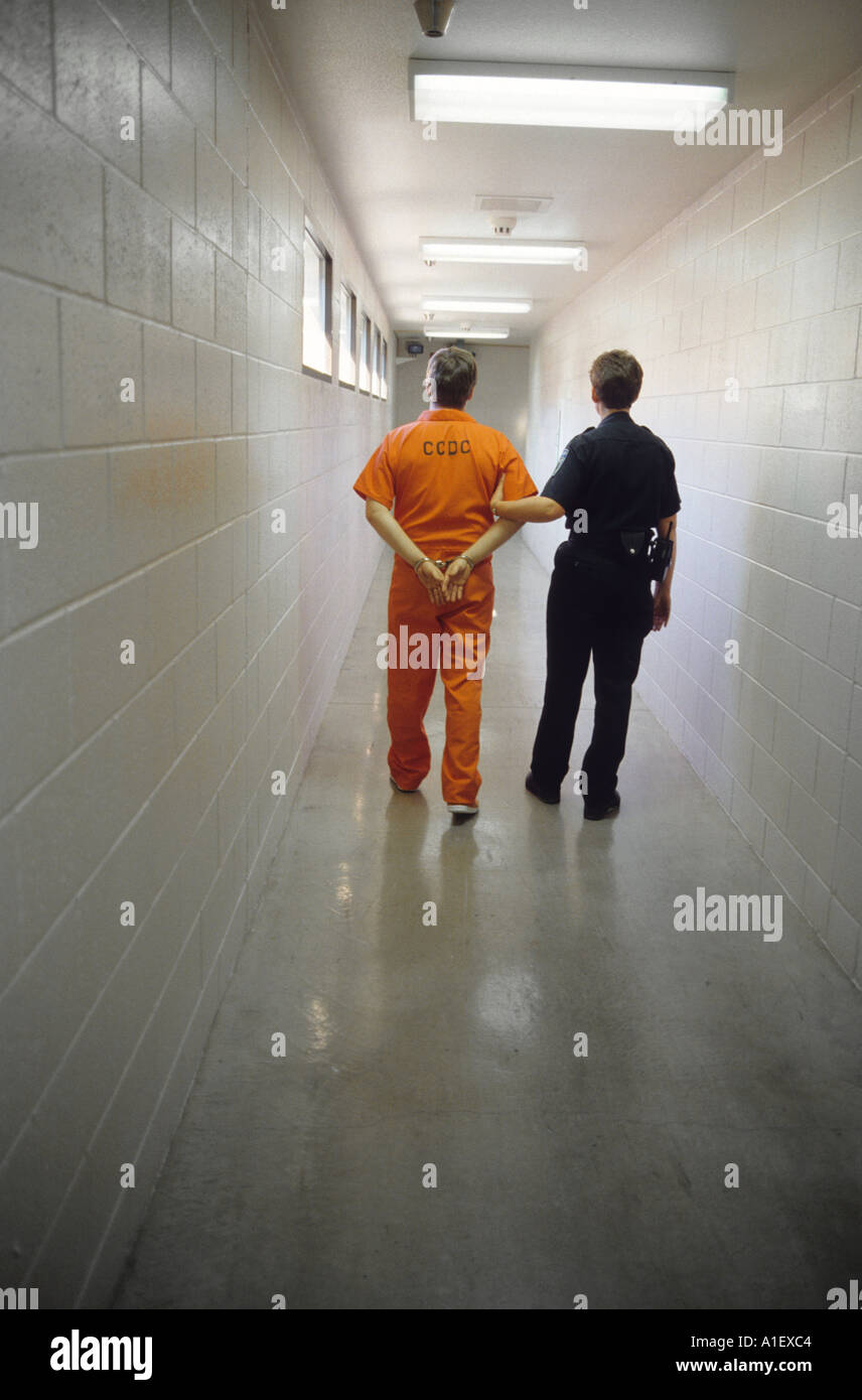 A handcuffed male inmate being escorted down a hall way by a jail Stock ...