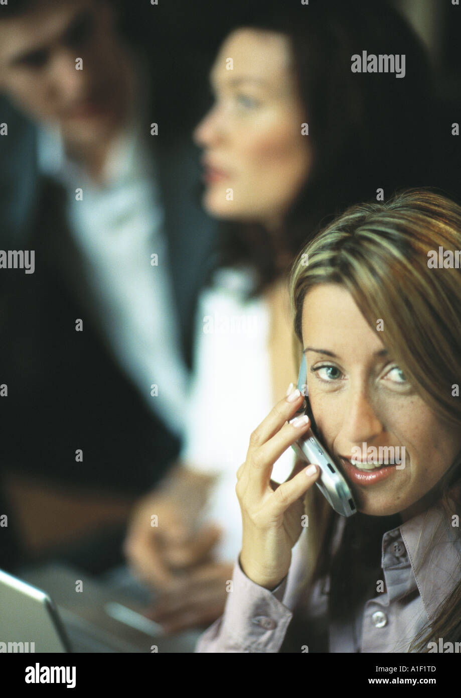 Businesswoman using cell phone in front of two co-workers Stock Photo ...