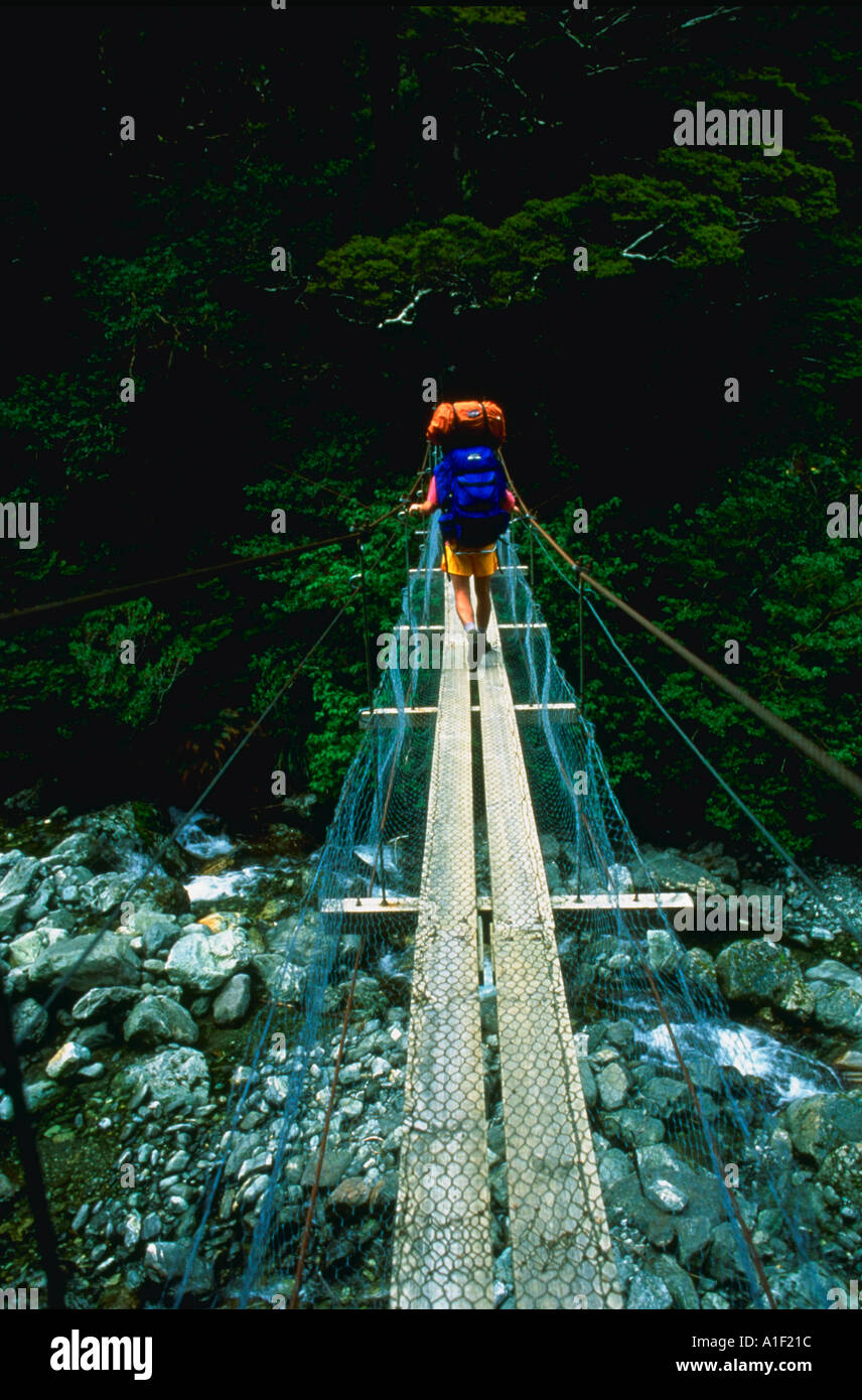 Hiker walking across swing bridge at headwaters of the Arthur River on ...